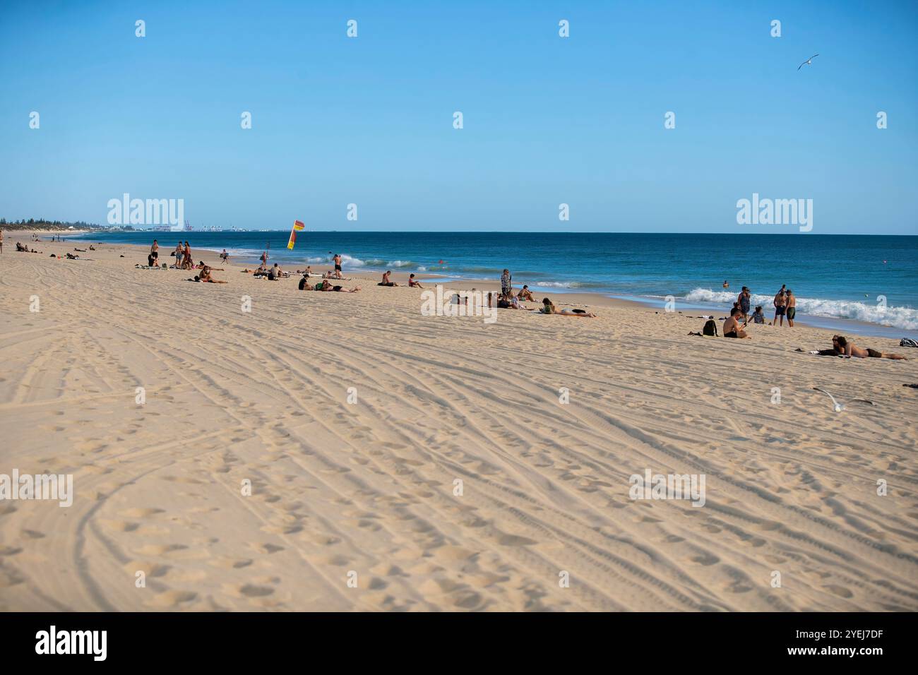 The photo shows a wide sandy beach with people scattered across the ...
