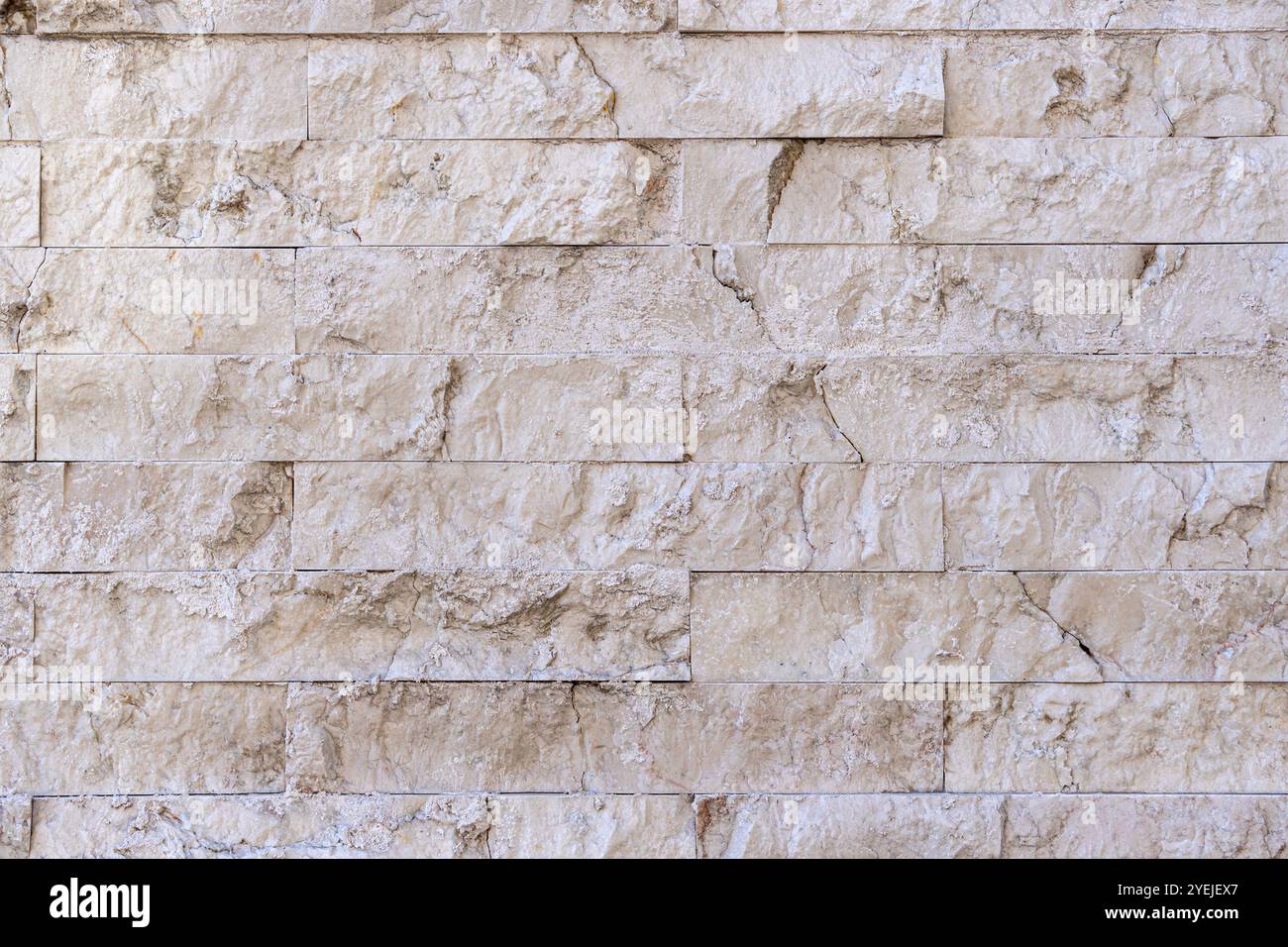 Stone wall made of beige tiles arranged in a staggered pattern. The ...