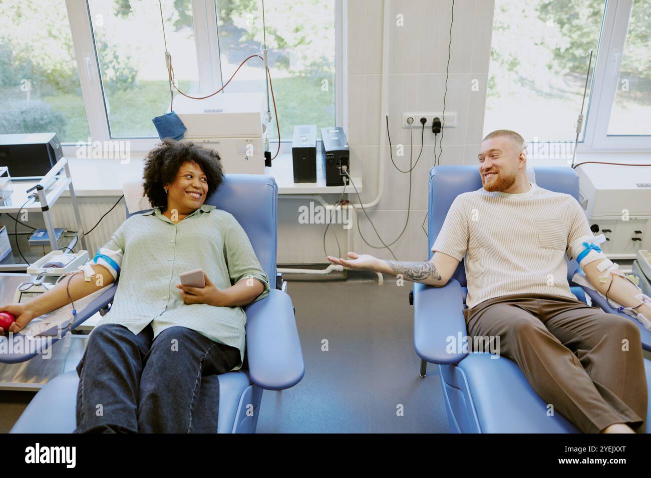 Two individuals sitting in medical chairs donating blood, engaging with ...