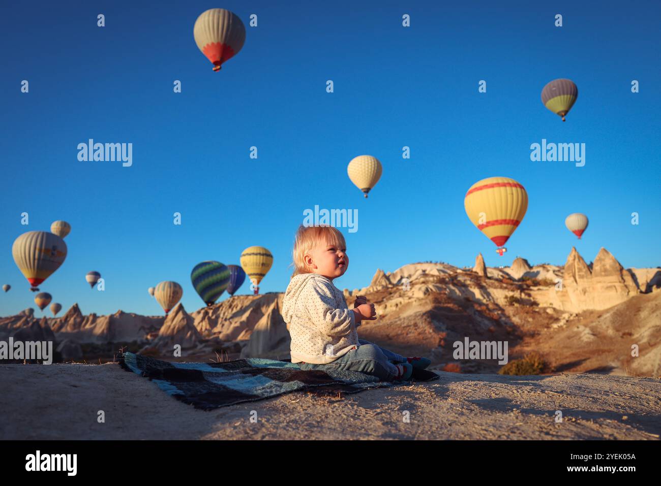 In Cappadocia a young child sits on a blanket captivated by colorful ...