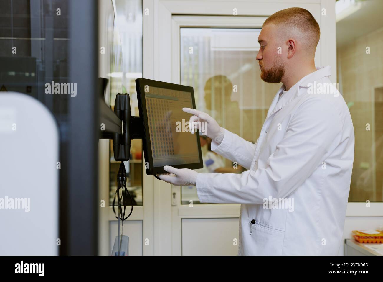 Scientist in white lab coat examining data on computer screen in modern ...