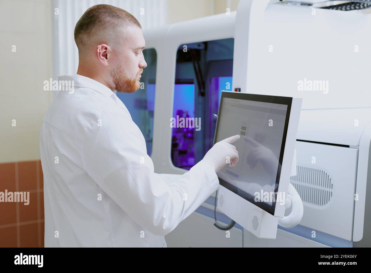 Male scientist in lab coat examining data on touchscreen monitor in modern laboratory ...