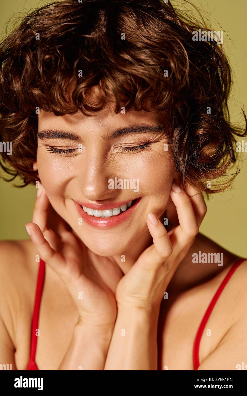 A young woman radiates joy, smiling with her eyes closed while touching ...