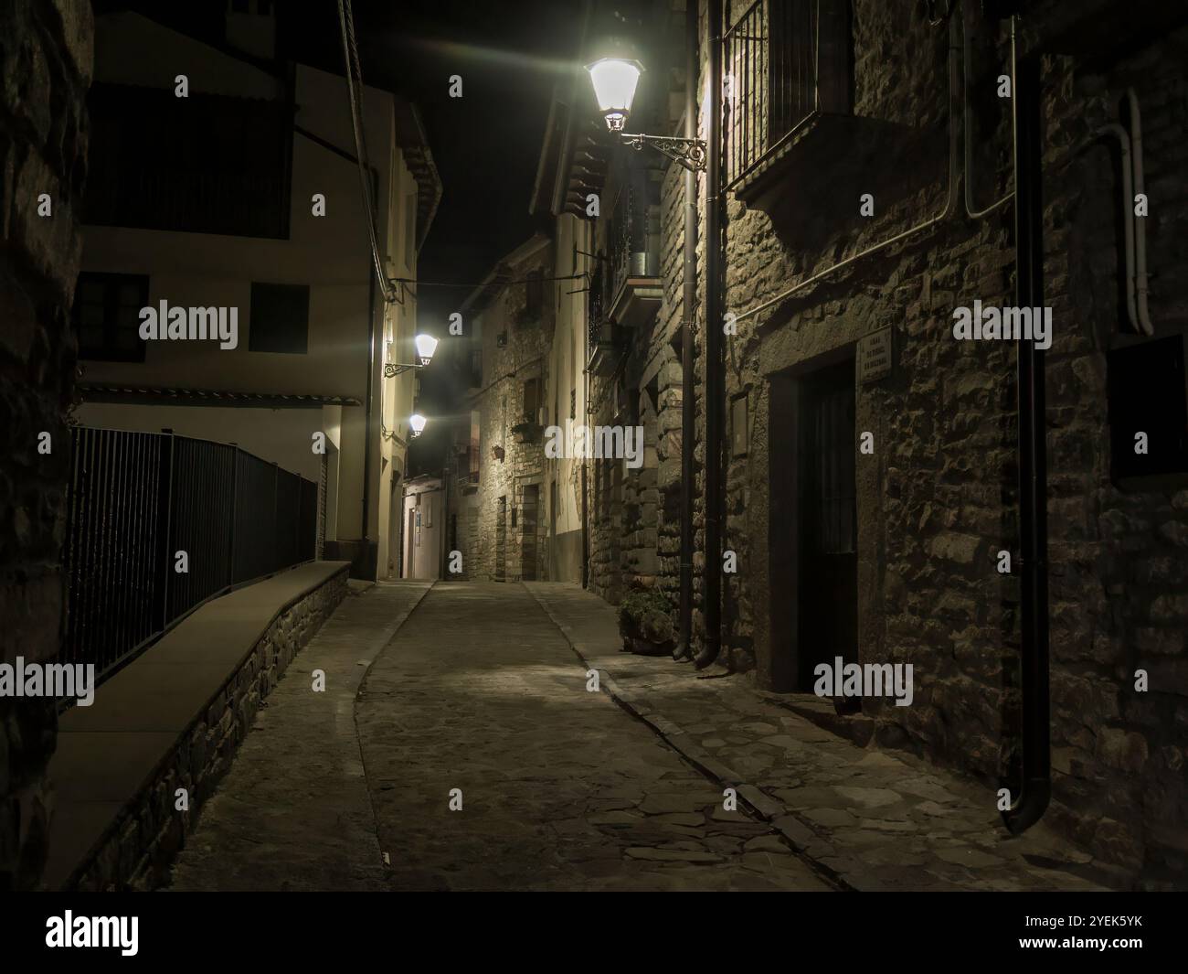 Narrow cobblestone alley illuminated by street lamps at night in a ...