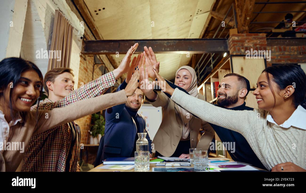 Team members from diverse backgrounds giving a high-five, celebrating ...