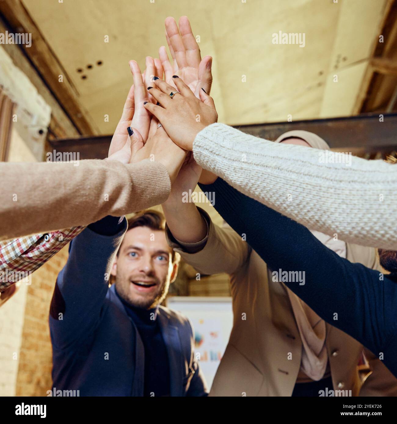 Team members from diverse backgrounds giving a high-five, celebrating ...