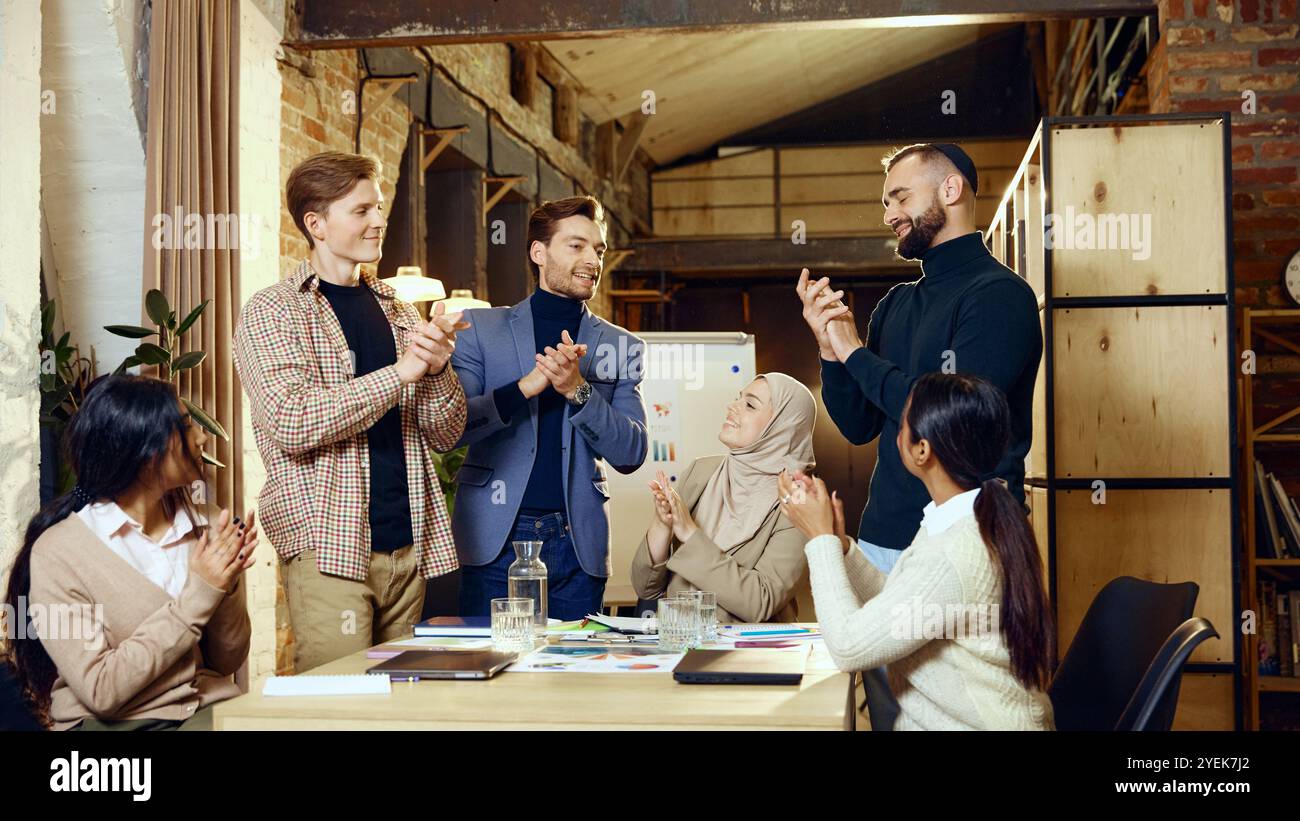 Colleagues from various cultural backgrounds applaud one another around ...