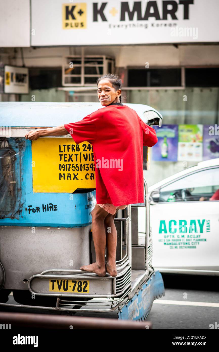 A young Filipino many holds on to the back of a jeepney bus speeding ...
