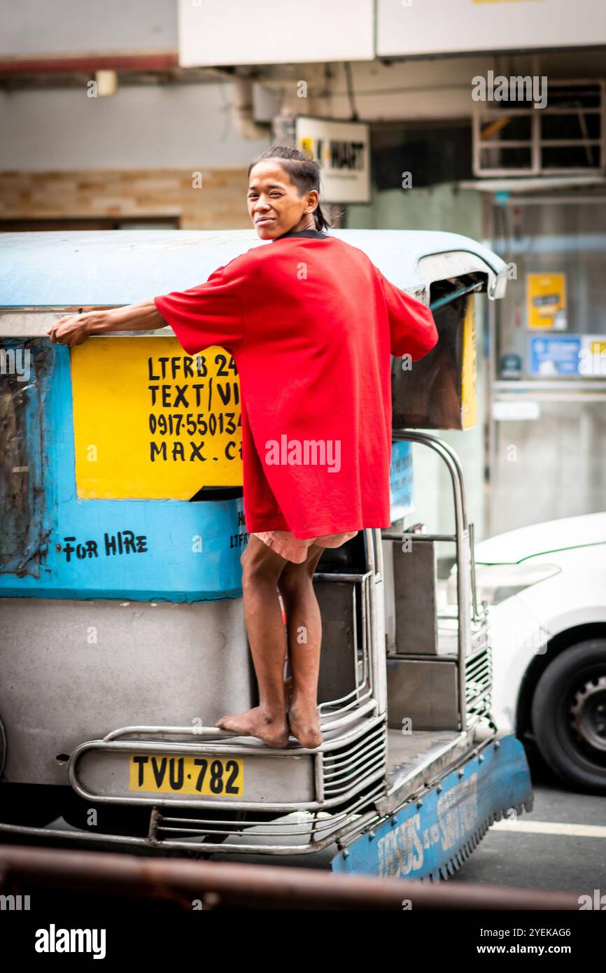 A young Filipino many holds on to the back of a jeepney bus speeding ...