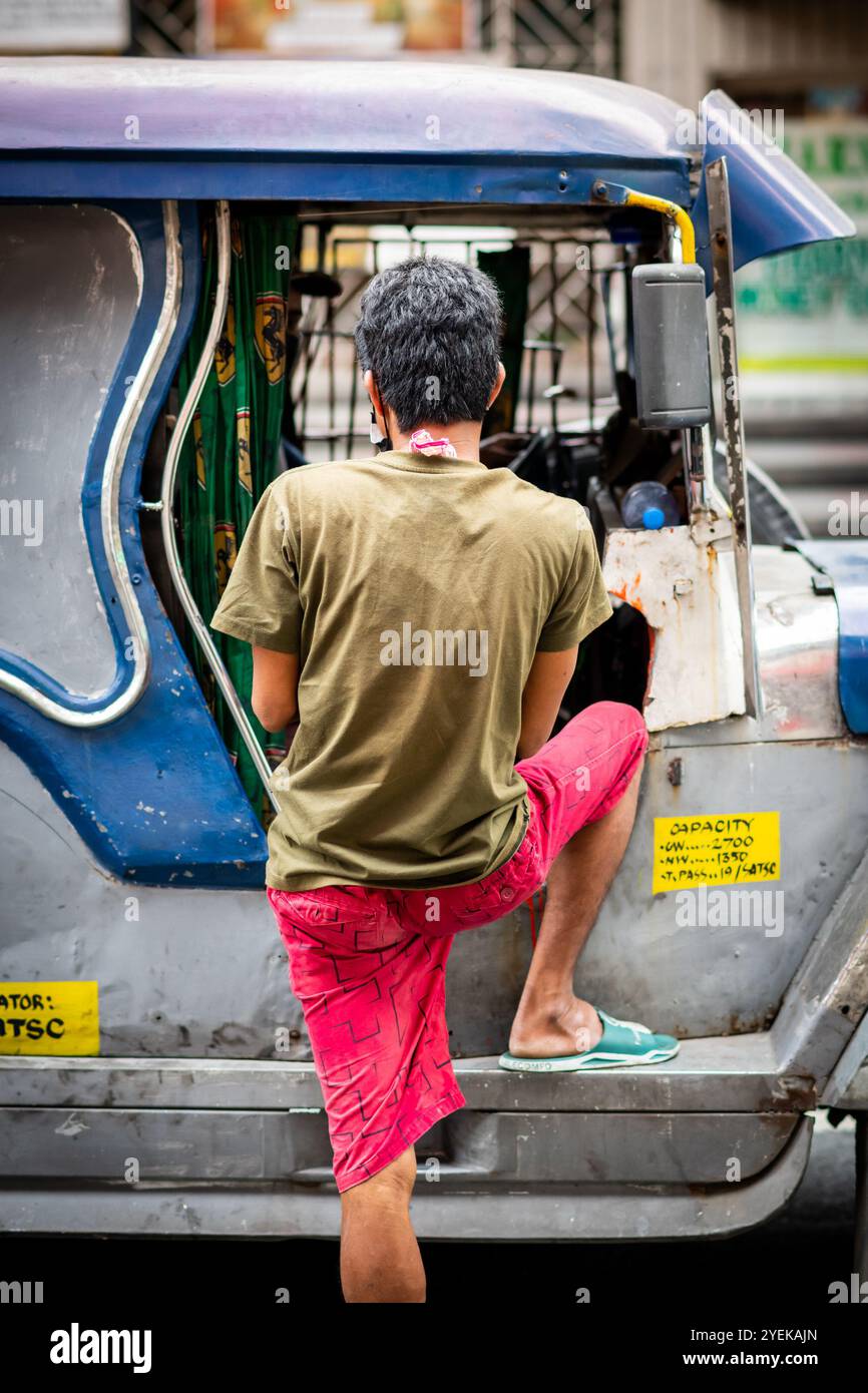 A young Filipino jeepney driver mounts a jeepney bus in Manila City ...