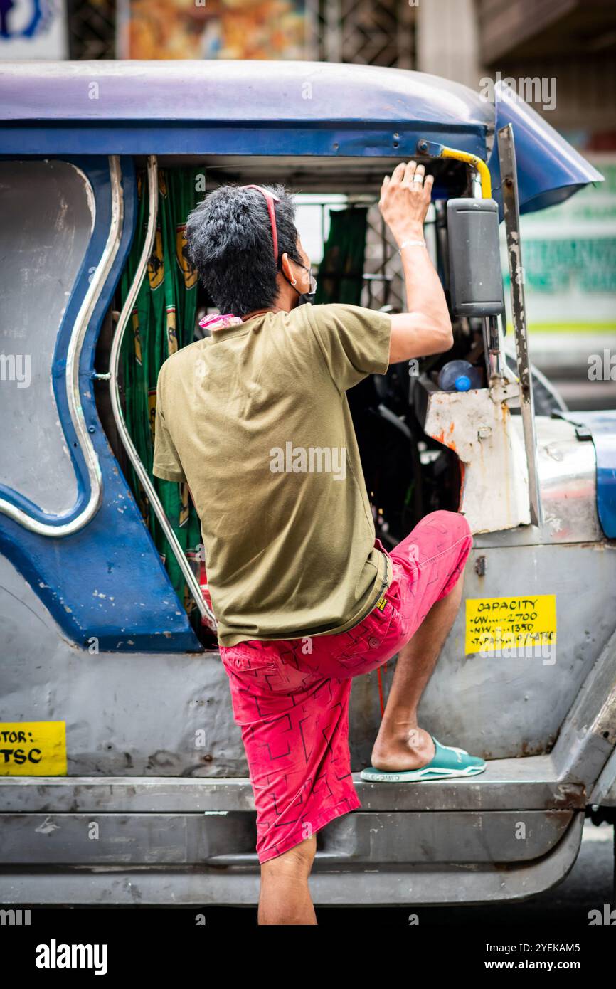 A young Filipino jeepney driver mounts a jeepney bus in Manila City ...