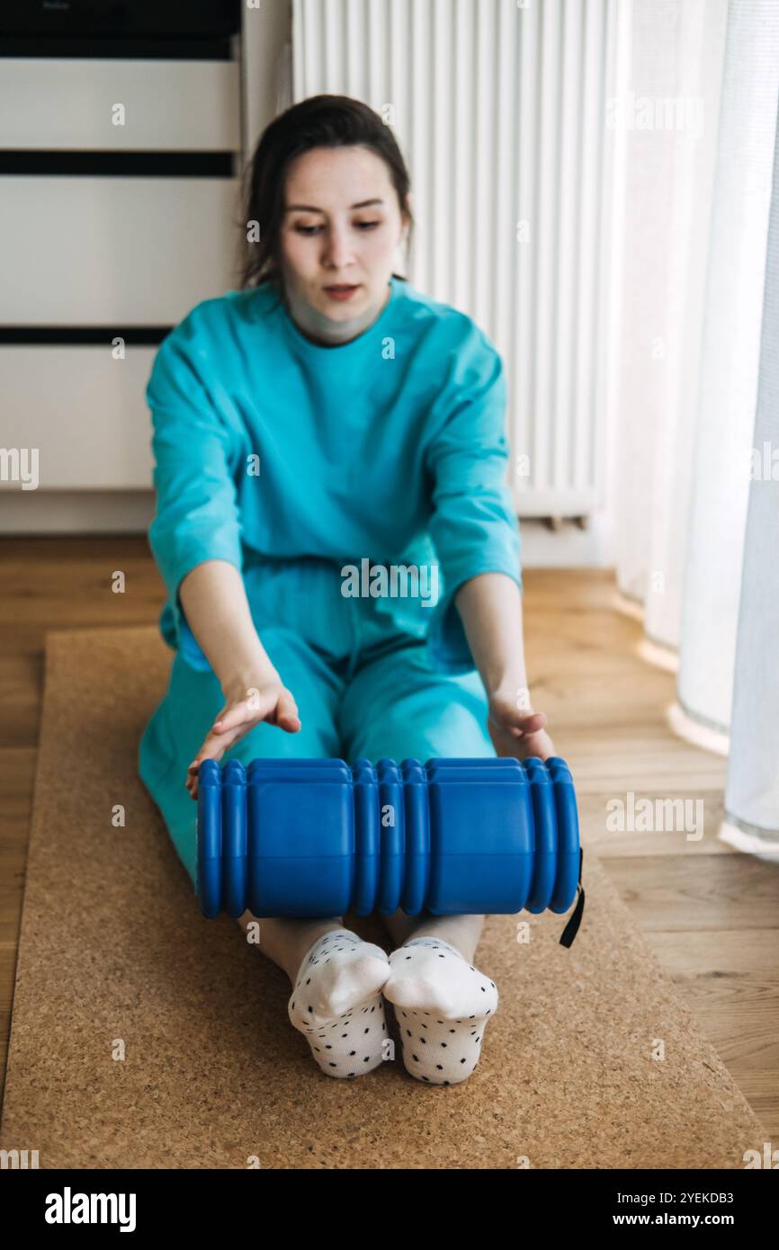 Young woman in blue clothing using foam roller for myofascial release ...