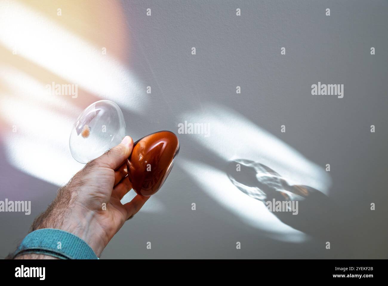 Hand holding a unique glass and wooden object casting intricate shadows ...