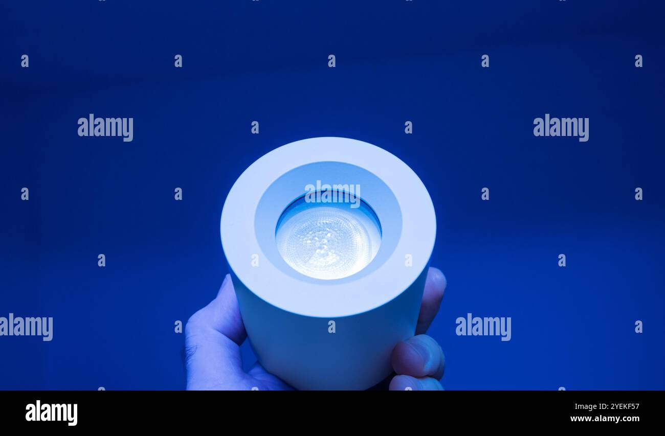 A hand holding an LED downlight illuminated in a blue light, creating a ...