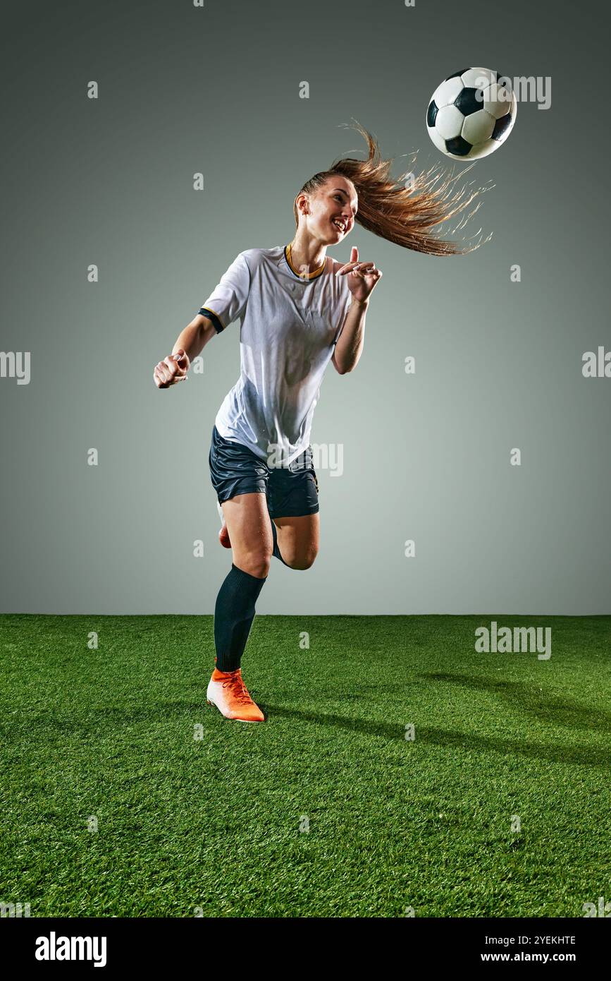 Female soccer player kicking ball with head. Woman in wet uniform ...