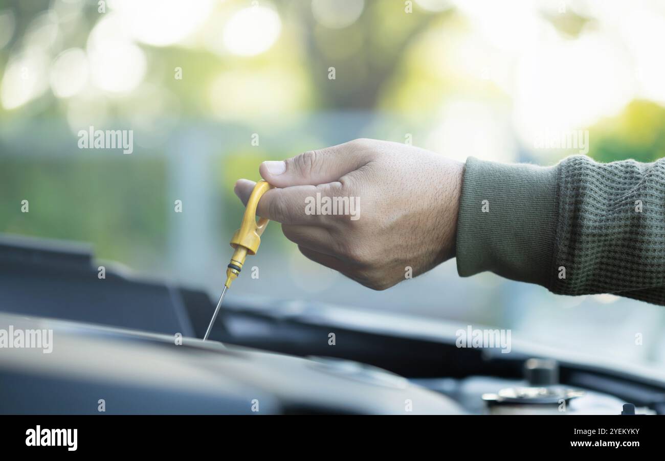 A car owner pulls out the dipstick to check engine oil levels, highlighting the importance of ...
