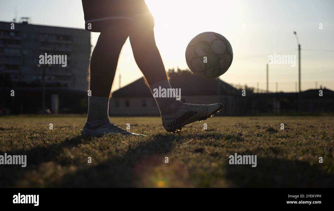 Legs of young man kicking ball at green field. Male feet of ...