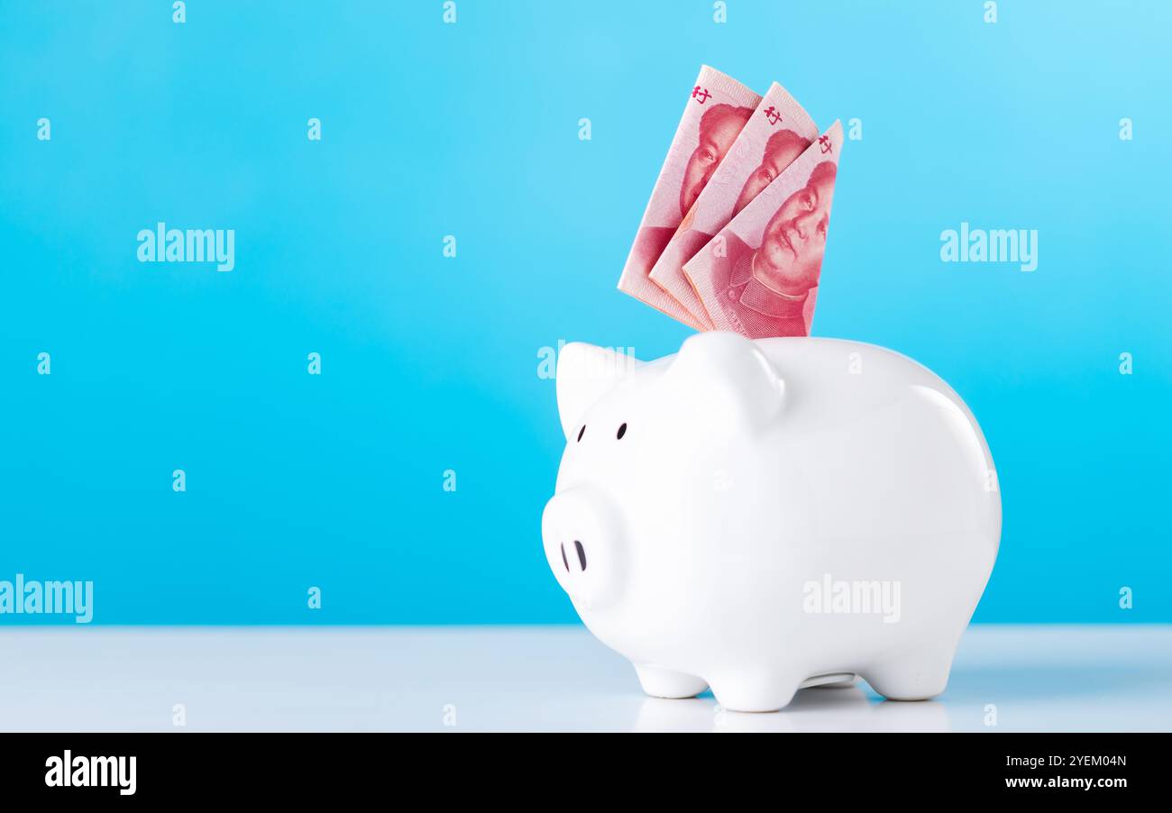 Hand holding a 100 Yuan note, dropping it into a white piggy bank, with ...