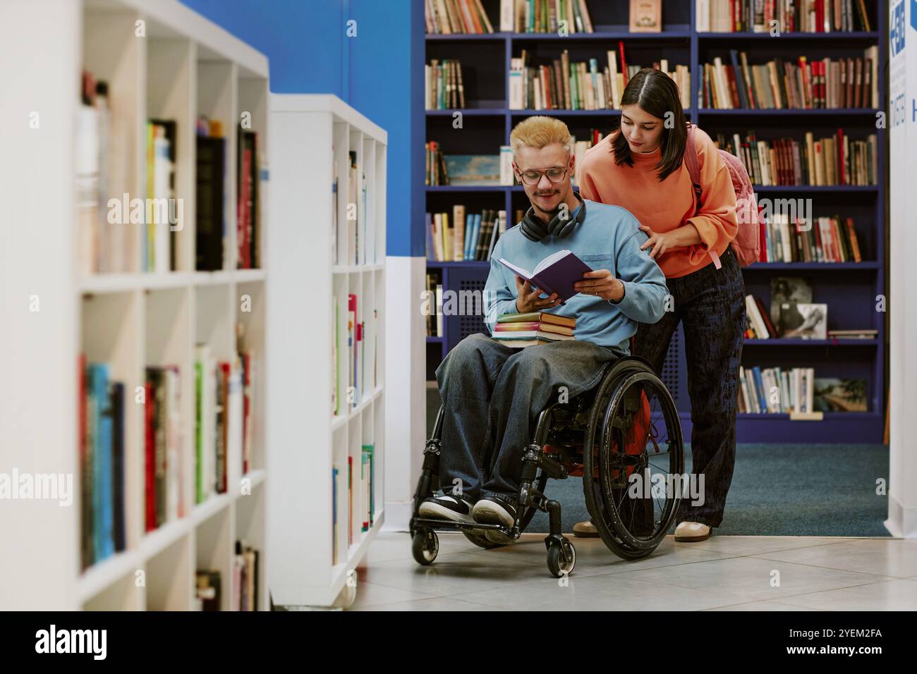 Young man in a wheelchair reading book with assistance of young woman ...