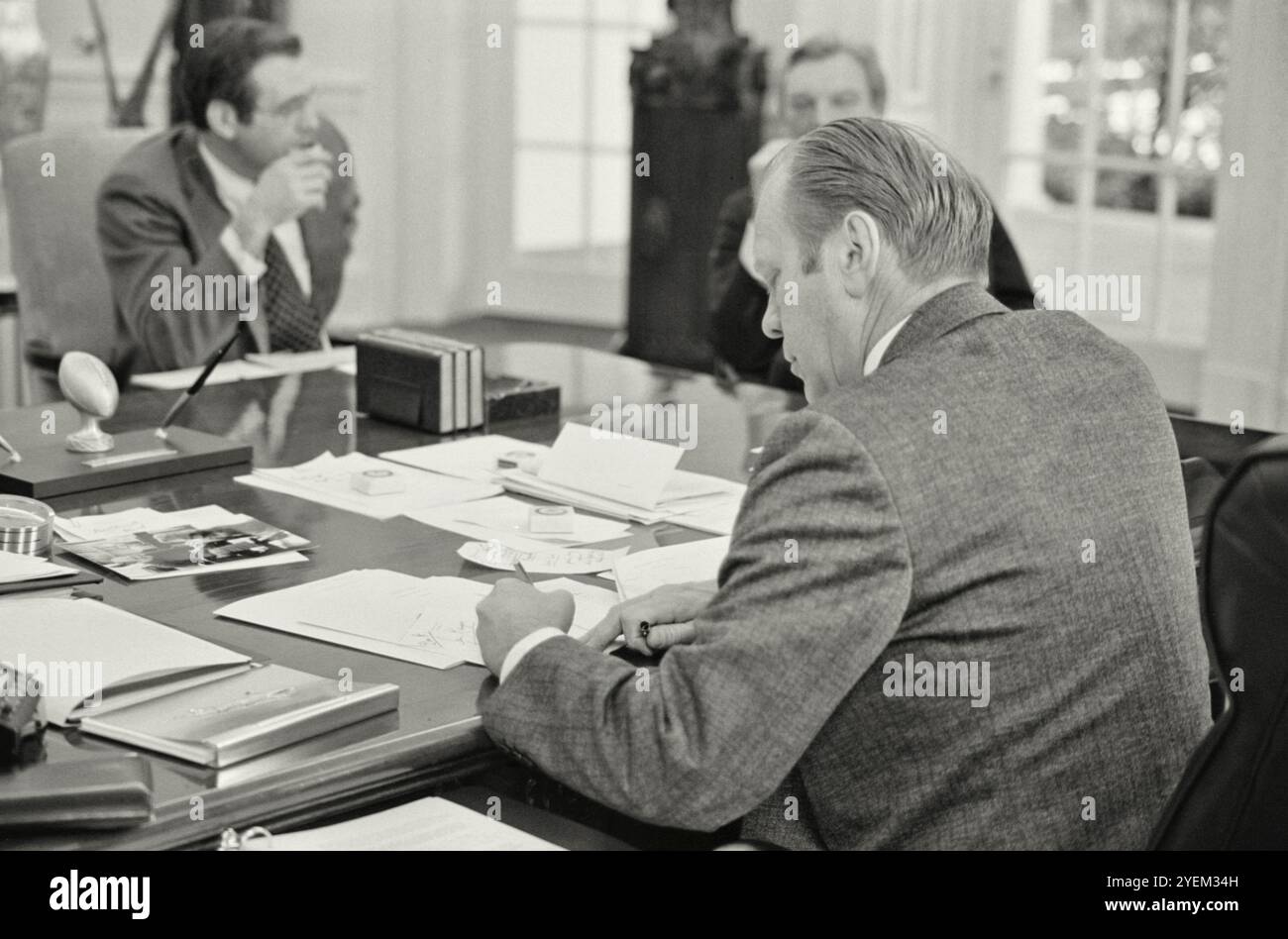 President Gerald Ford writing at his desk during a staff meeting at the ...