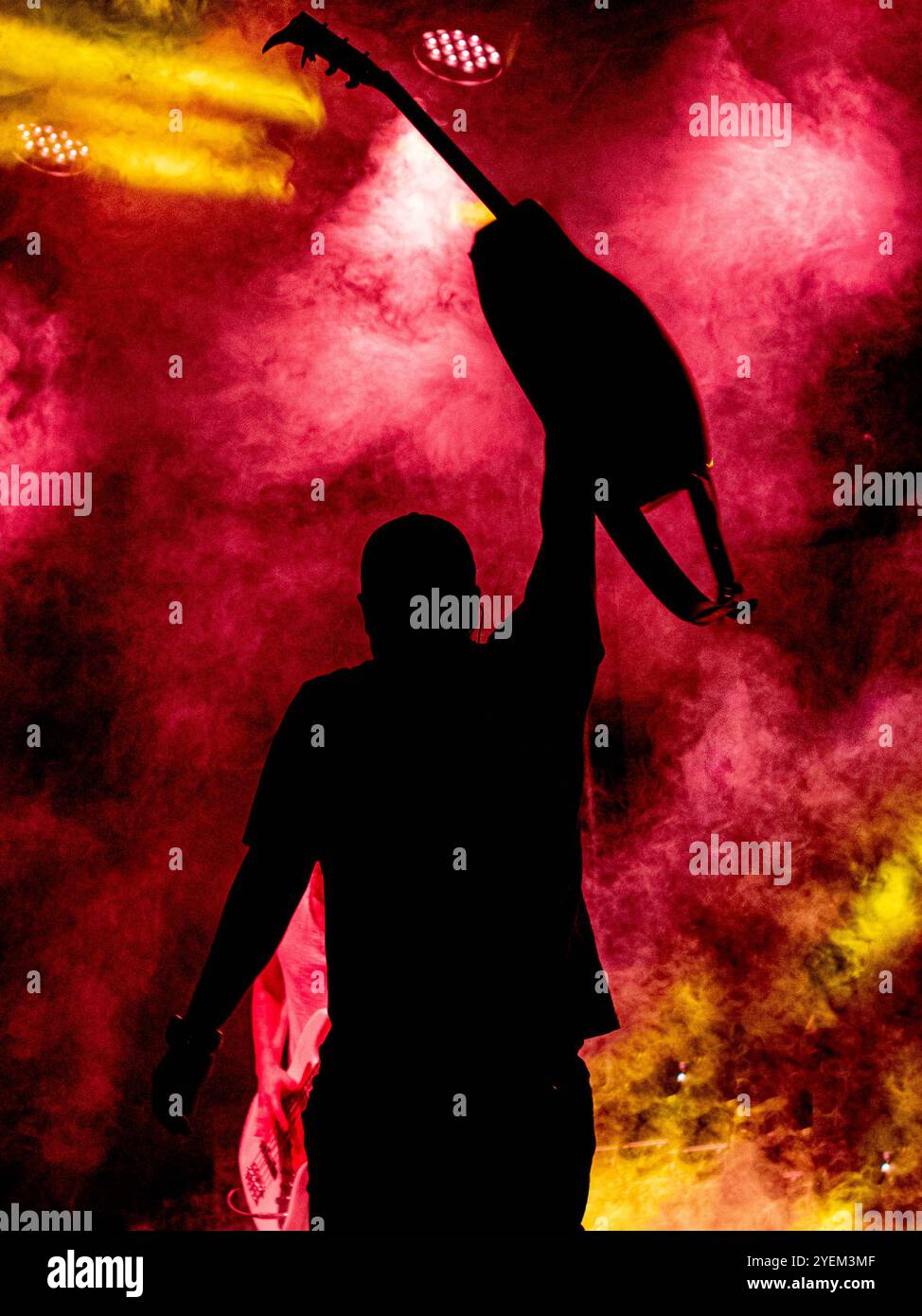 The frontman of a band raises his guitar during a concert, surrounded ...