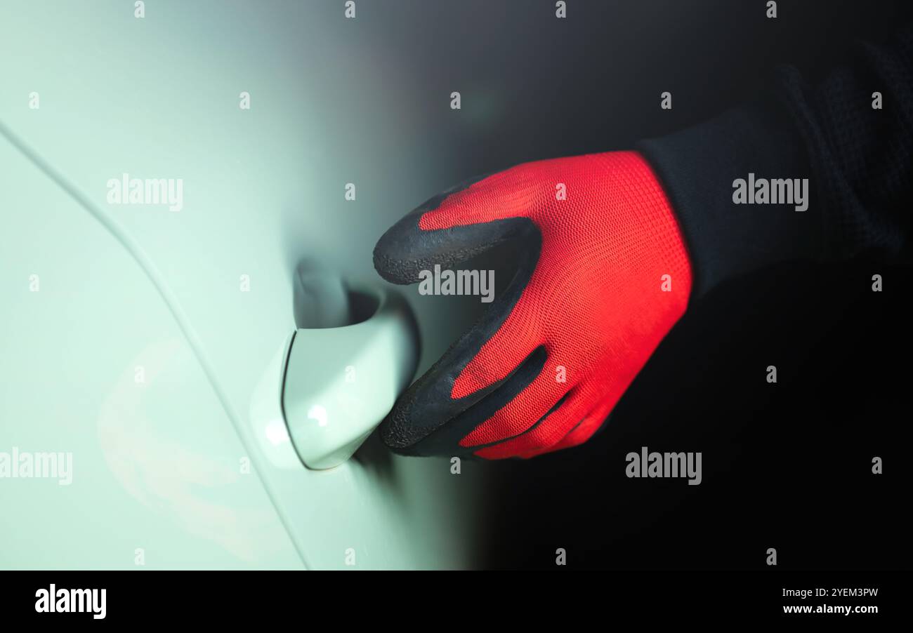 A man's gloved hand holding a screwdriver, attempting to pry open a car ...