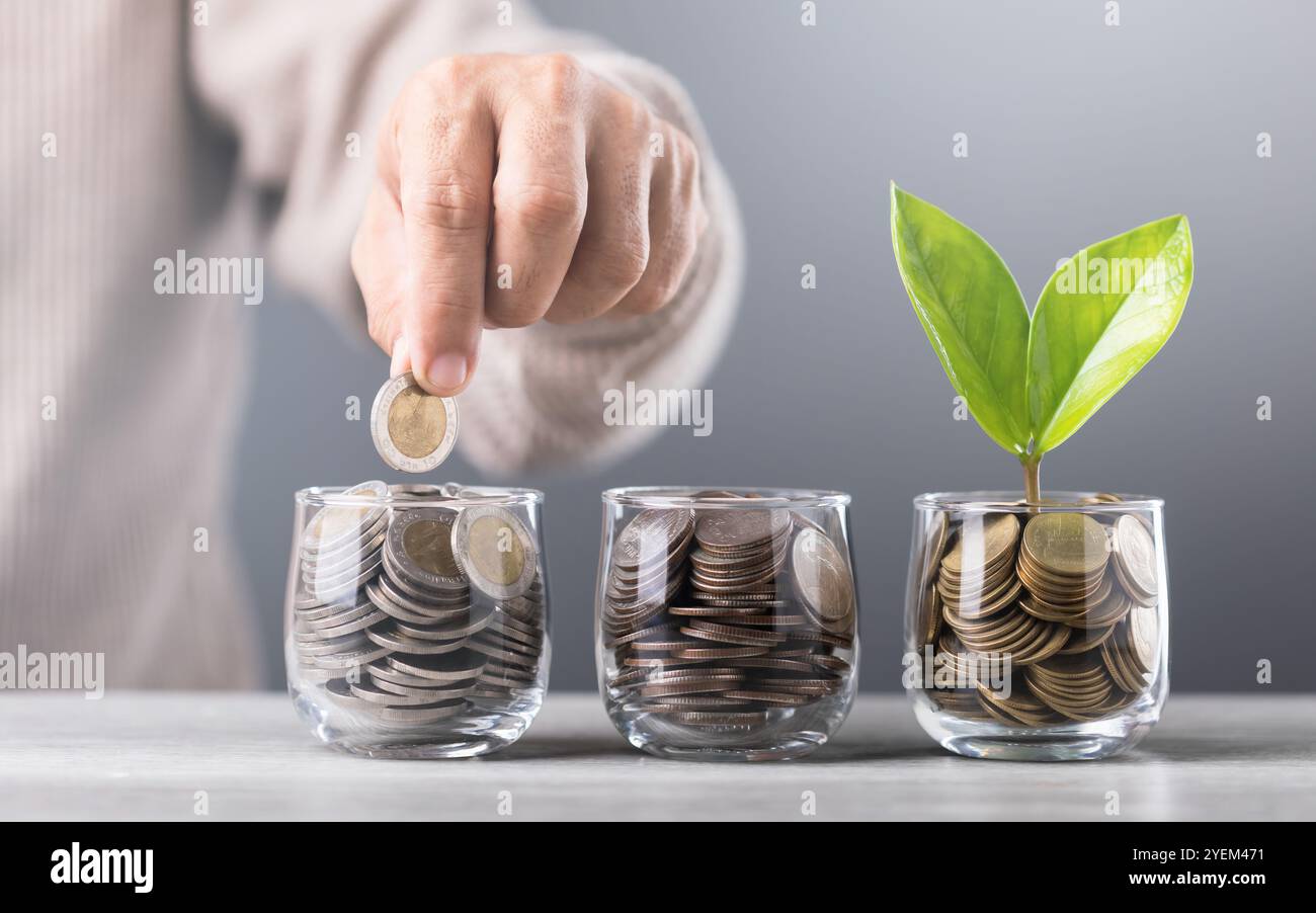 Hand drops coins into a glass jar, with stacks of coins arranged from ...