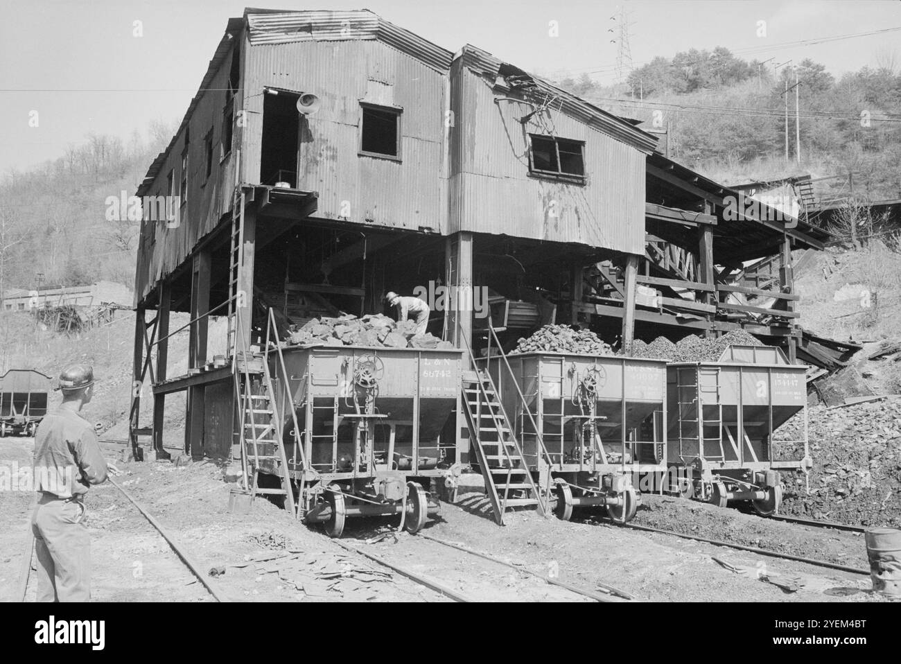 Coal miner on cart loaded with coal? at a building next to tracks ...