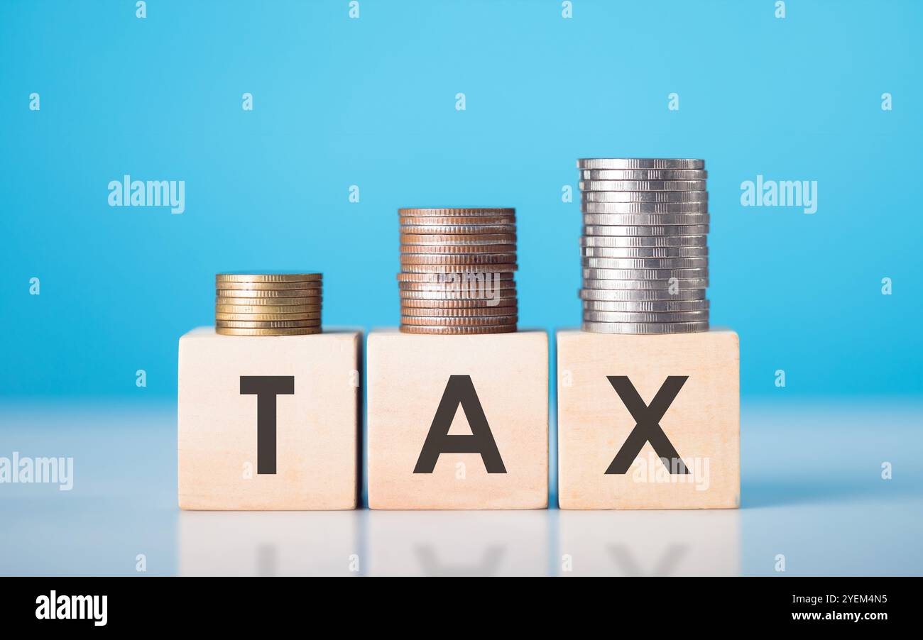 TAX is write on a wooden block next to a stack of coins. Against light ...