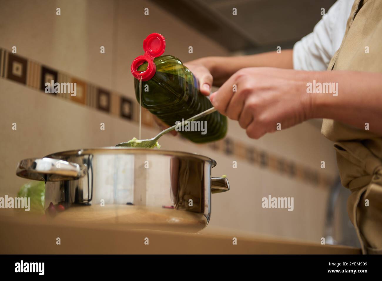 A close-up view of a person pouring oil into a cooking pot ...