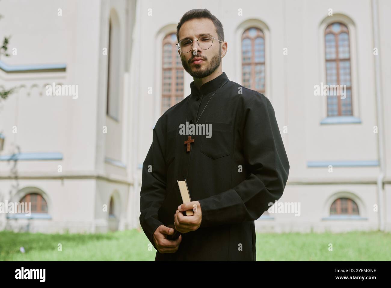 Portrait of young Caucasian priest dressed in black robe and wearing ...