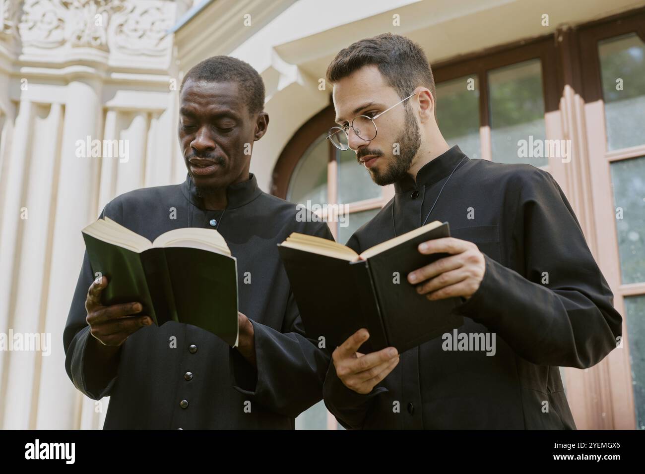 Mature African American and Caucasian priests reading holy book ...