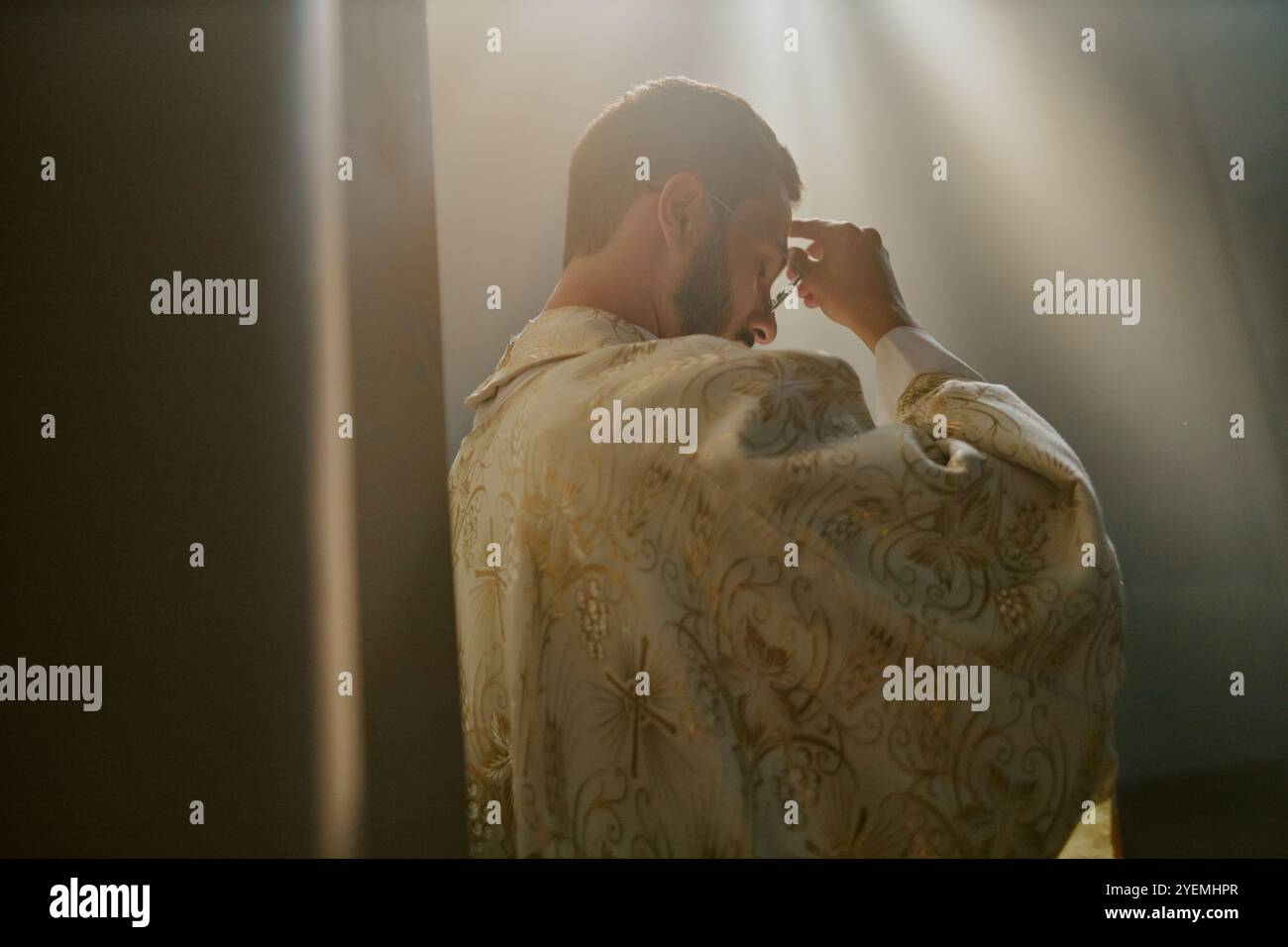 Back view of Caucasian priest in golden white robe adjusting his round ...