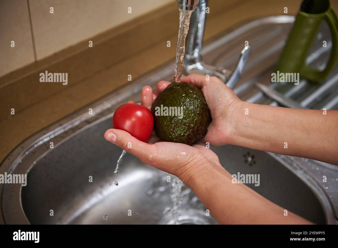 Close-up of hands washing a fresh avocado and tomato under running ...