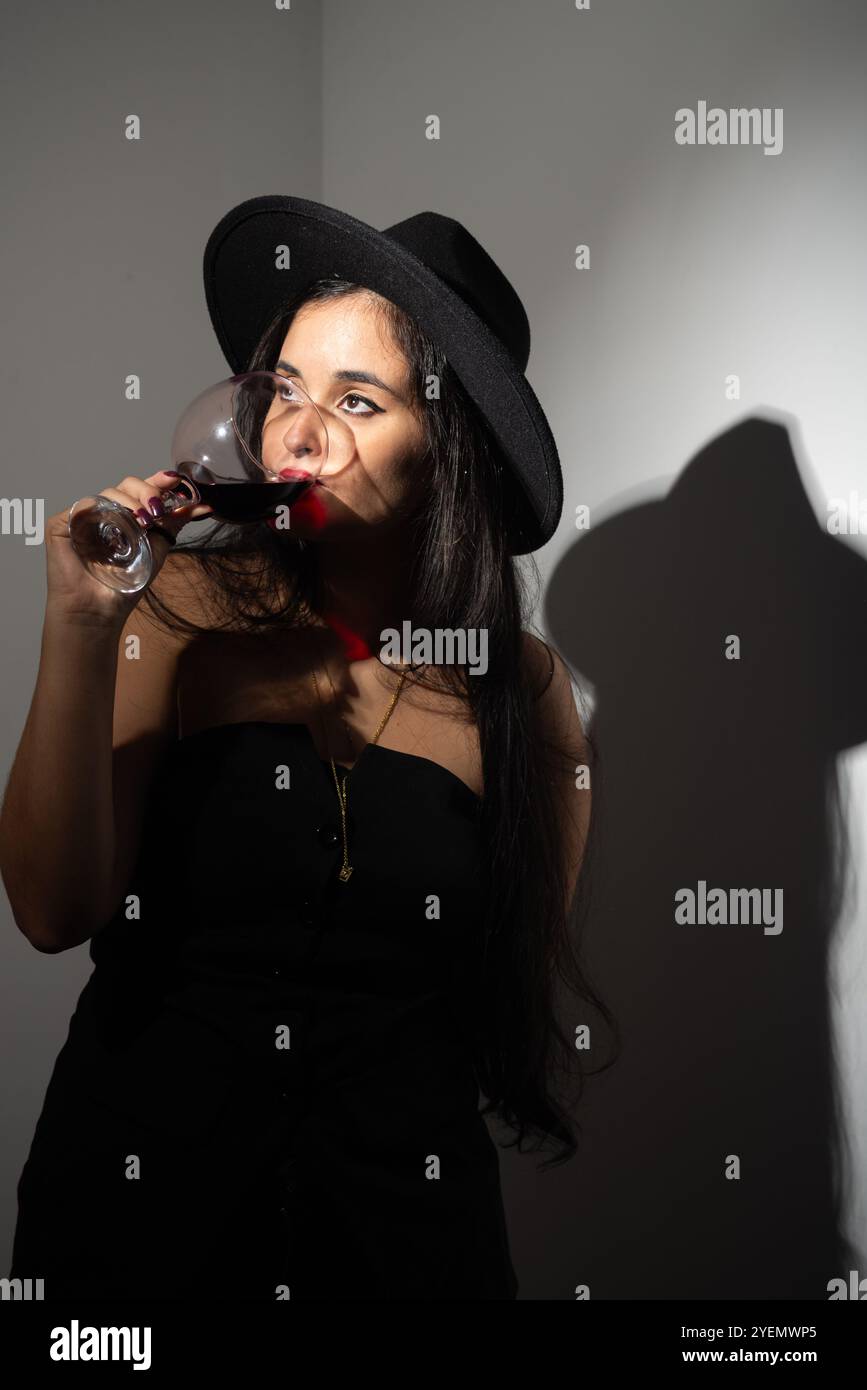 Beautiful woman in black dress and hat drinking wine from a glass cup ...