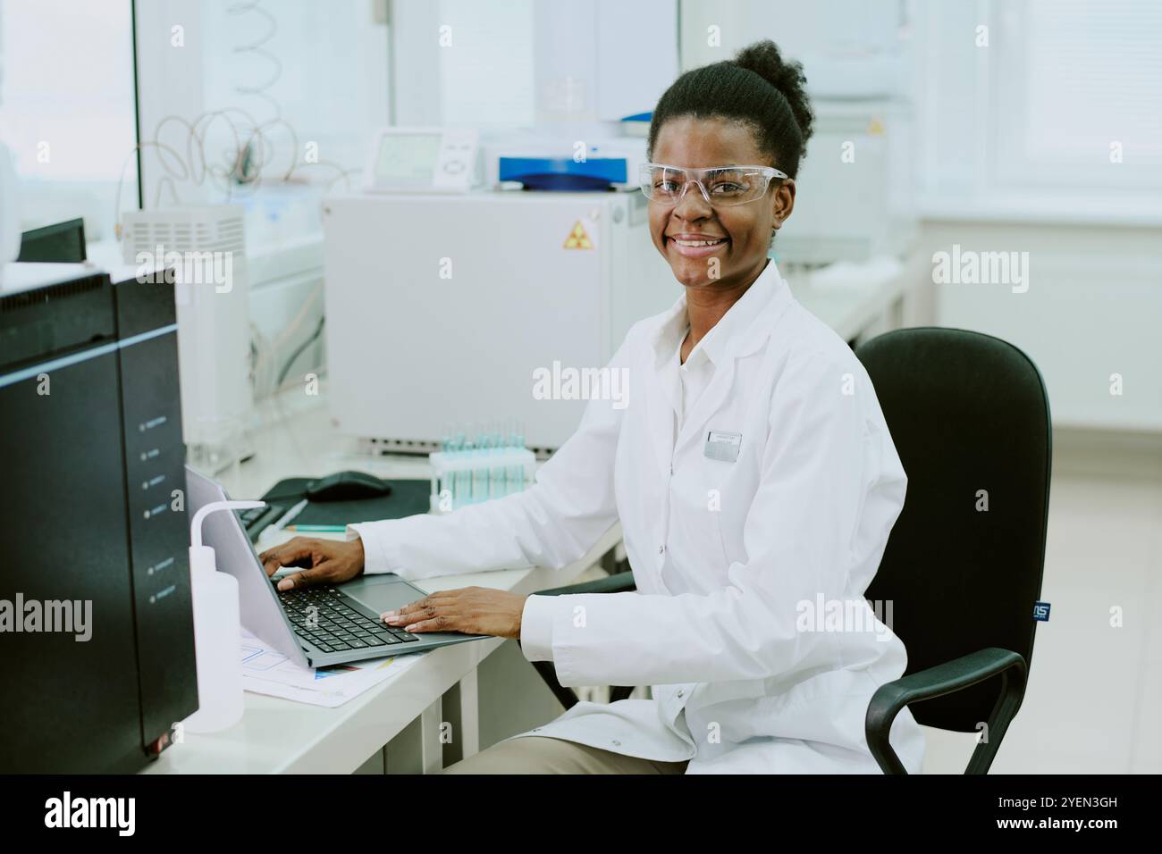 Smiling scientist facing laptop while working in laboratory, wearing ...