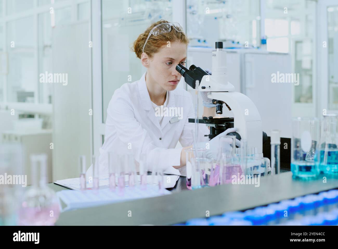 Scientist wearing lab coat carefully examining samples under microscope ...