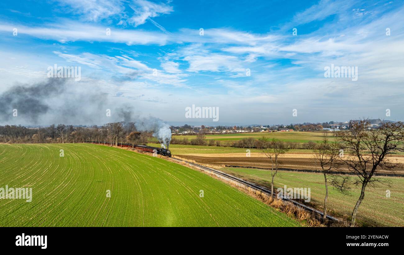 A steam train chugs along a track cutting through vibrant green fields ...