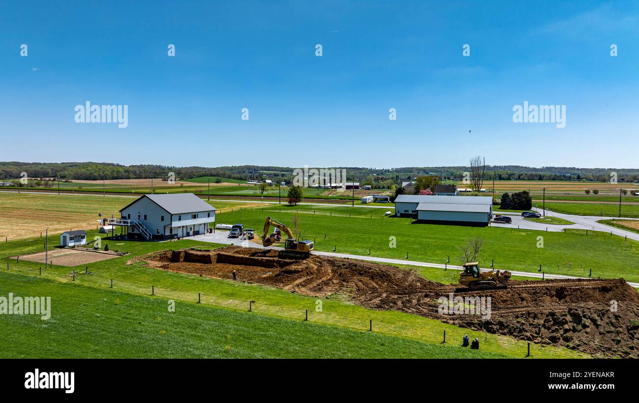 Heavy machinery works on a construction site near a house, surrounded ...