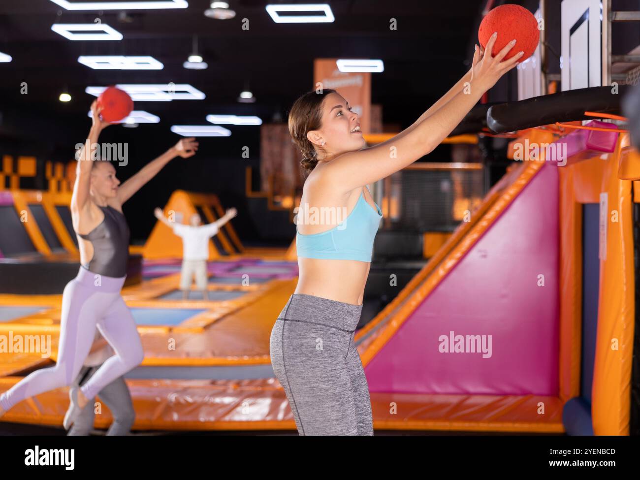 Young woman throwing ball in basket high jumping in trampoline arena ...