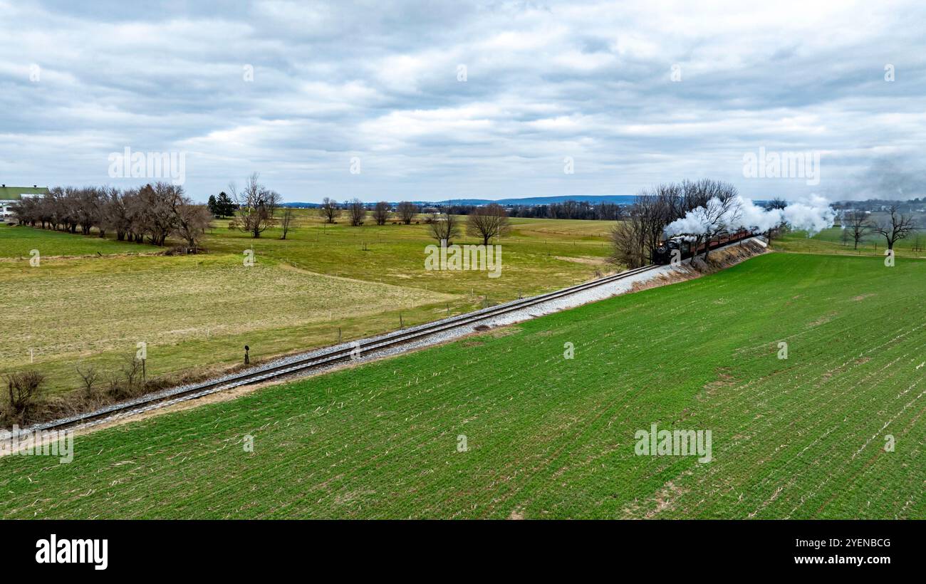 A vintage steam train chugs along railway tracks winding through ...