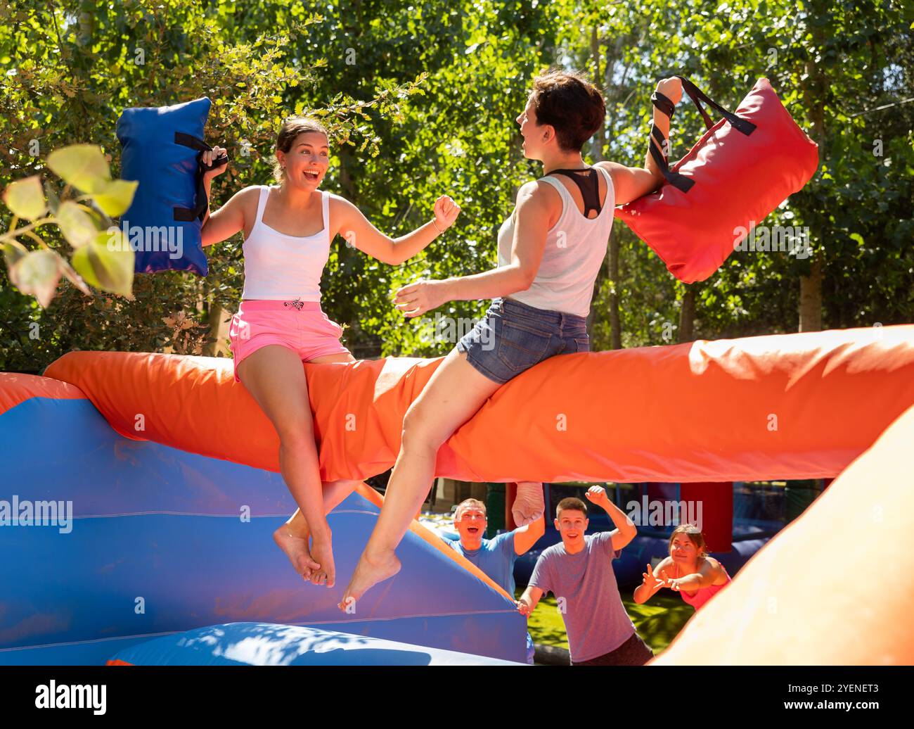 Happy girl funny pillow fighting on inflatable log with female friend ...