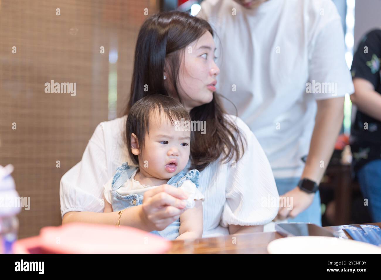 A 1 year old Taiwanese girl enjoying a meal with her parents, a man and ...