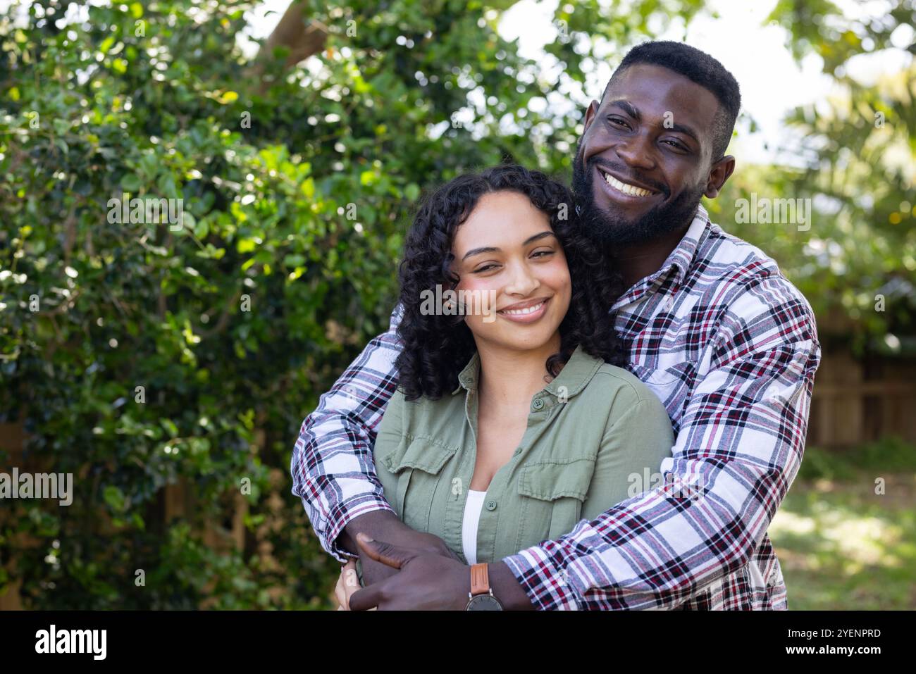 Happy multiracial couple embracing outdoors, smiling warmly in lush ...