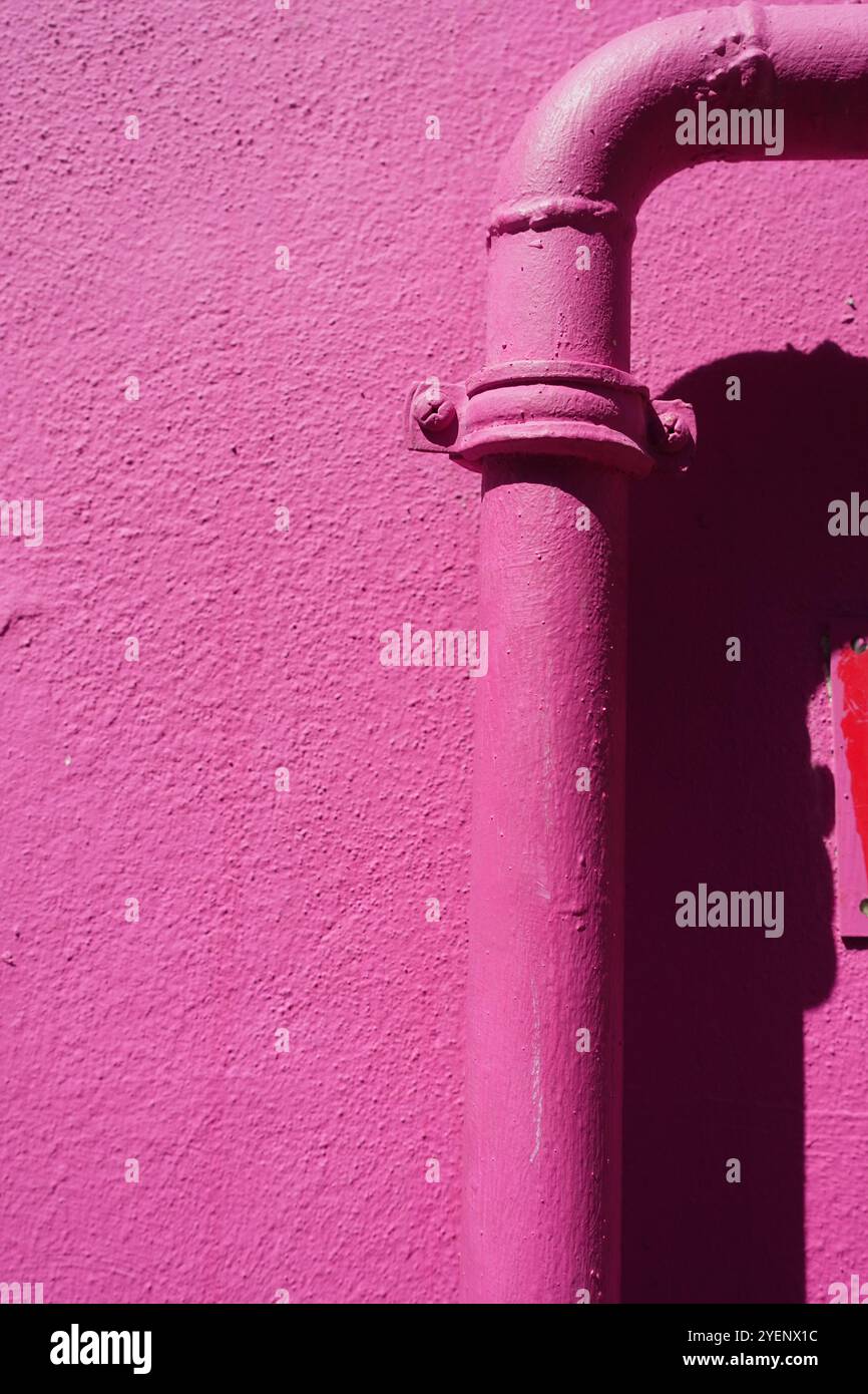 Pink wall with pipe, illuminated by sun, displaying modern urban design ...