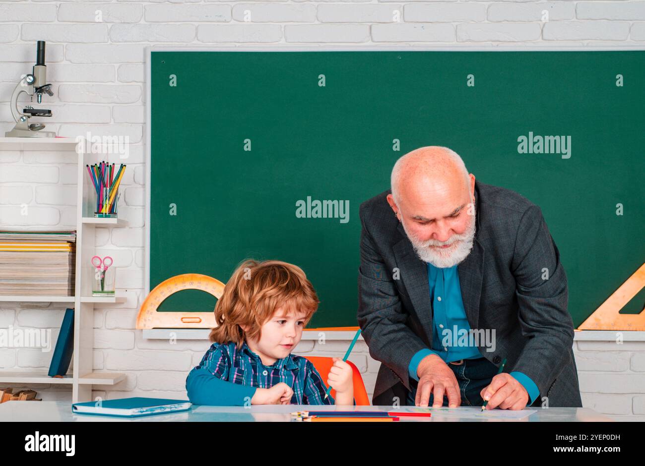 Pupil and Teacher in classroom. Senior teacher with pupil at back of ...