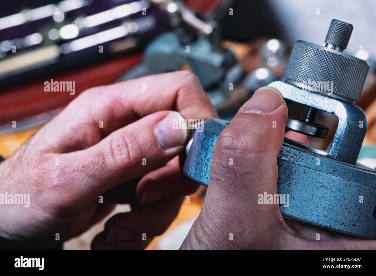 Close-up of watchmaker’s hands using a textured tool on a workbench ...