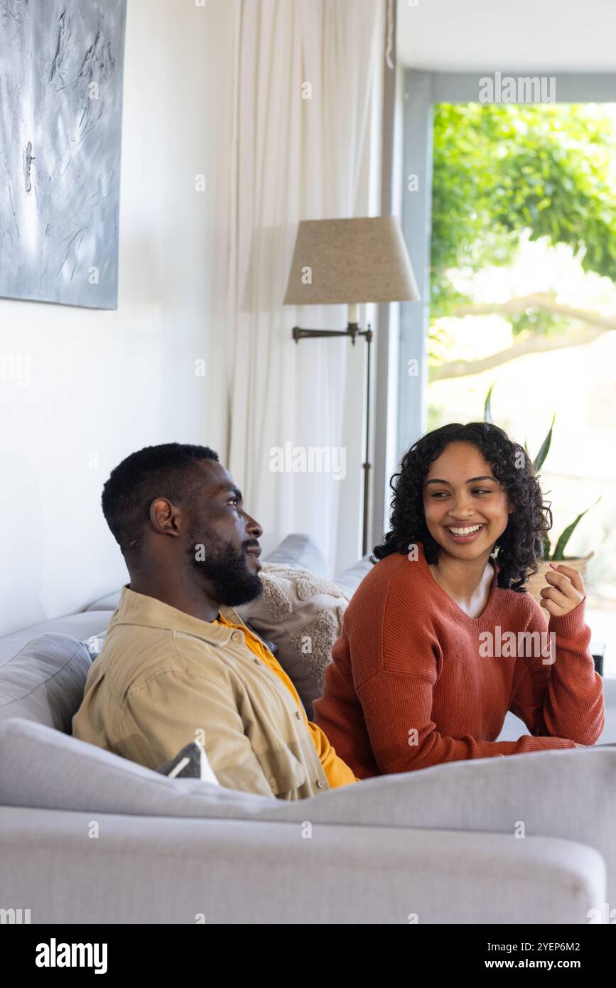 Happy multiracial couple relaxing on couch at home, enjoying conversation and laughter ...