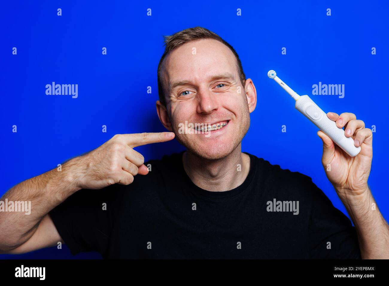 Portrait of a young handsome man brushing his teeth with an ultrasonic modern toothbrush. Oral ...