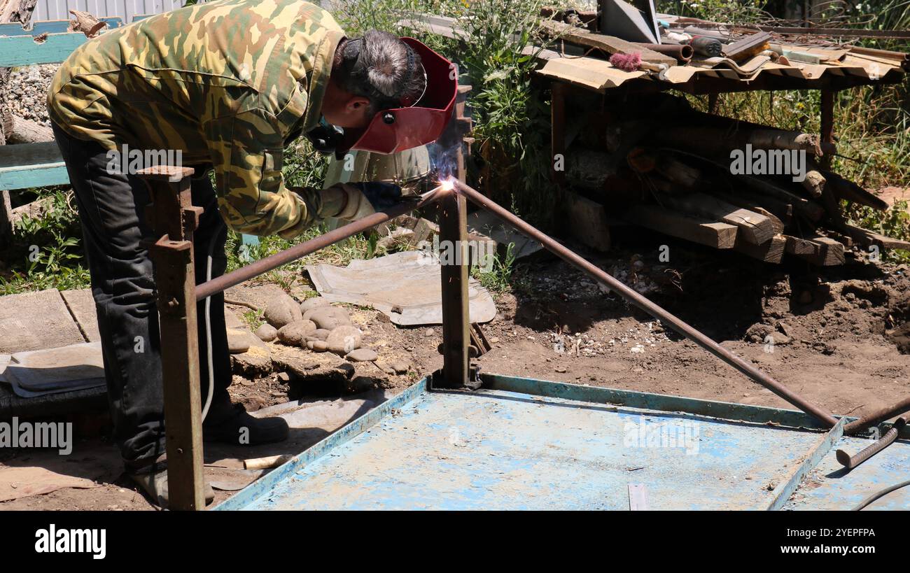 welder in red protective helmet and green jacket leaning over metal ...
